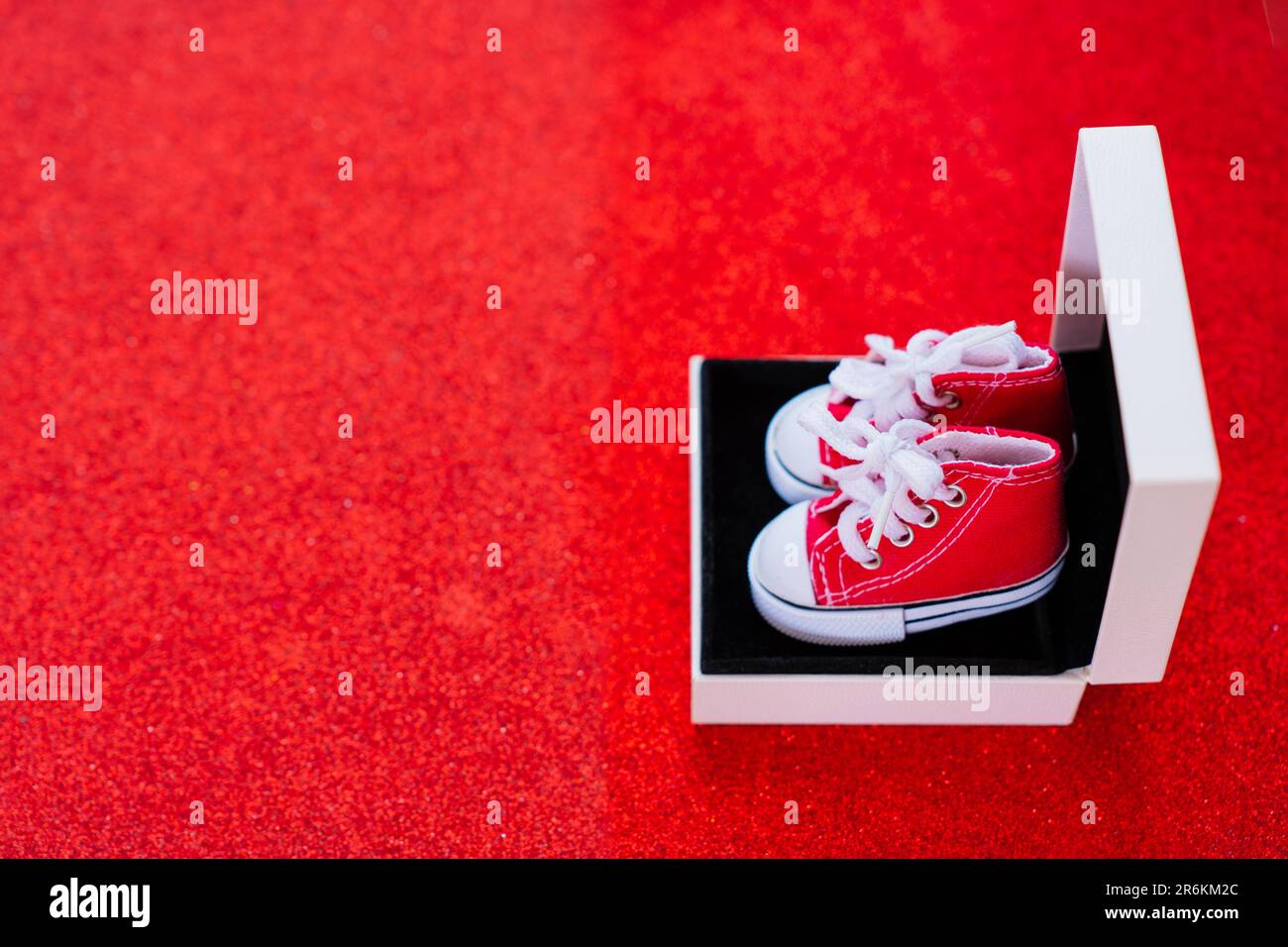 Pair of toy-size red canvas shoes resting inside a small gift box, set ...