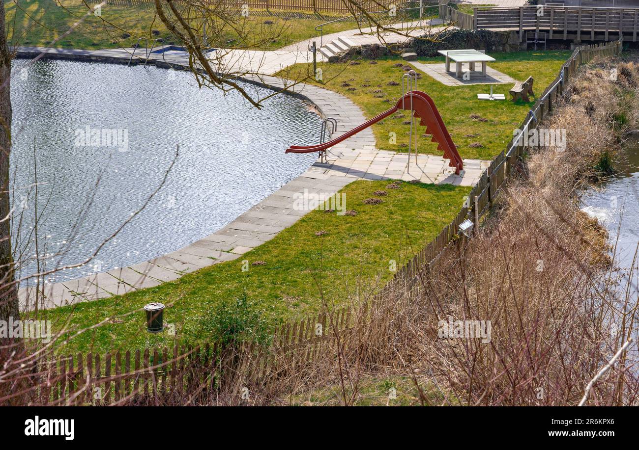 A view of a sparkling blue swimming pool featuring a red slide on one ...