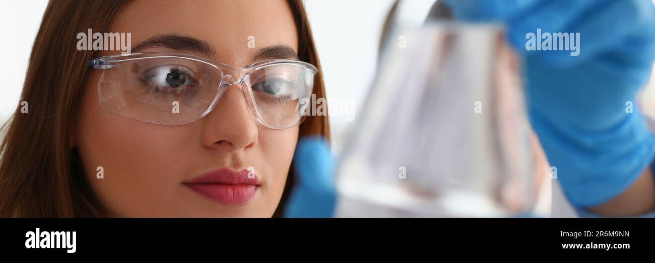 Portrait of woman scientist in glasses holds flask with transparent ...