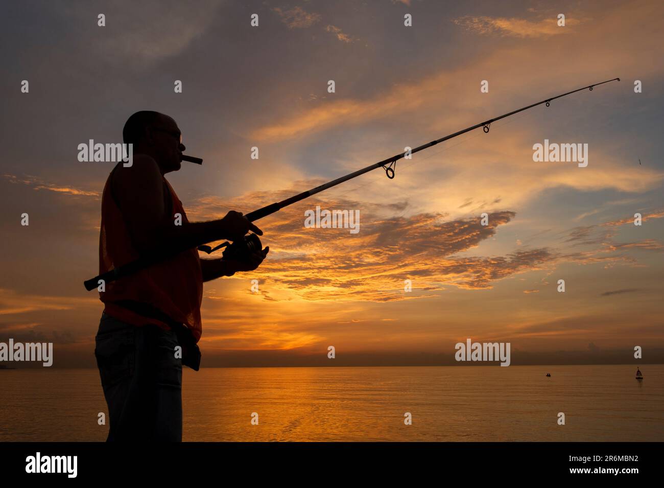 Havana, Cuba. Silhouette of a man fishing at sunset while smoking a ...