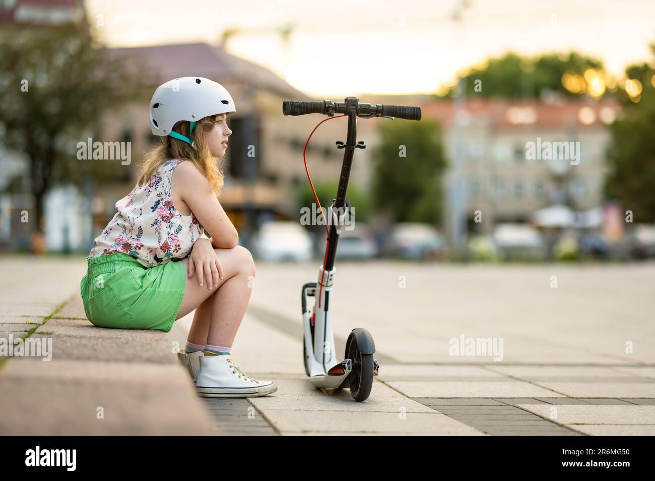 Adorable young girl riding her scooter in a city on sunny summer ...