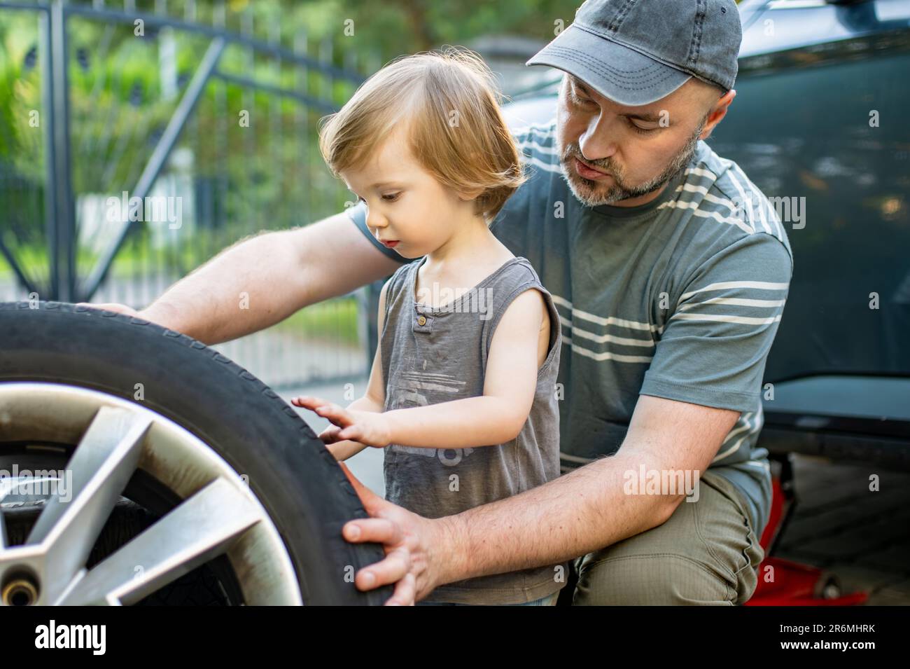 Cute toddler boy helping his father to change car wheels at their ...