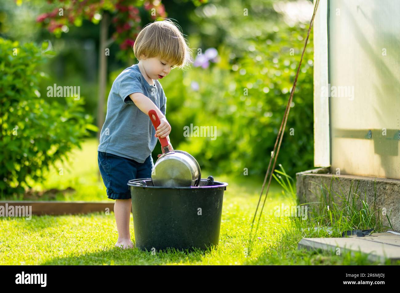 Cute blond little toddler playing with a cooking pot outdoors in the ...