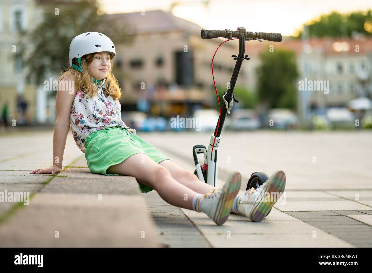 Adorable young girl riding her scooter in a city on sunny summer ...
