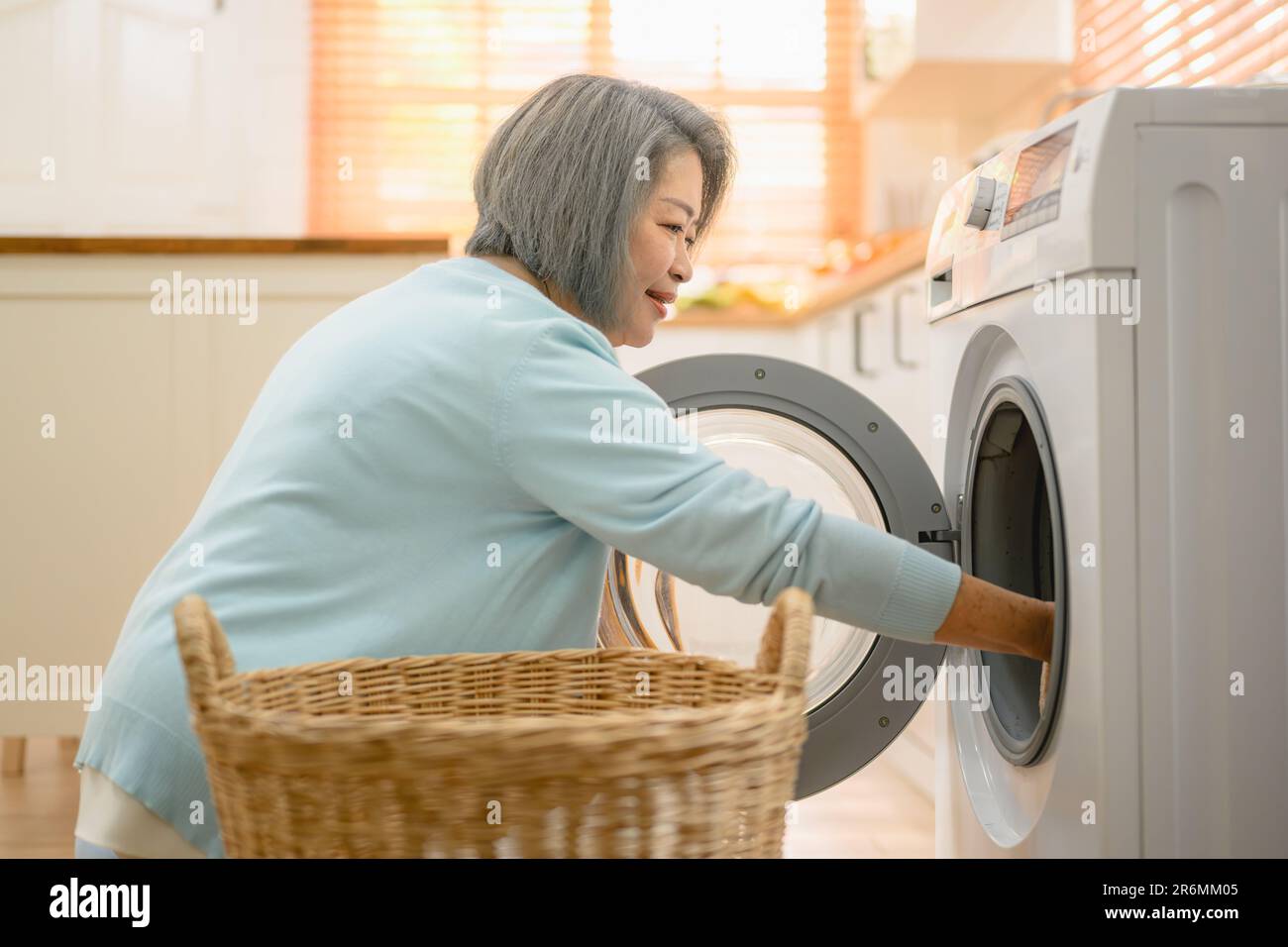 a beautiful senior woman, takes care of the laundry using a washing ...