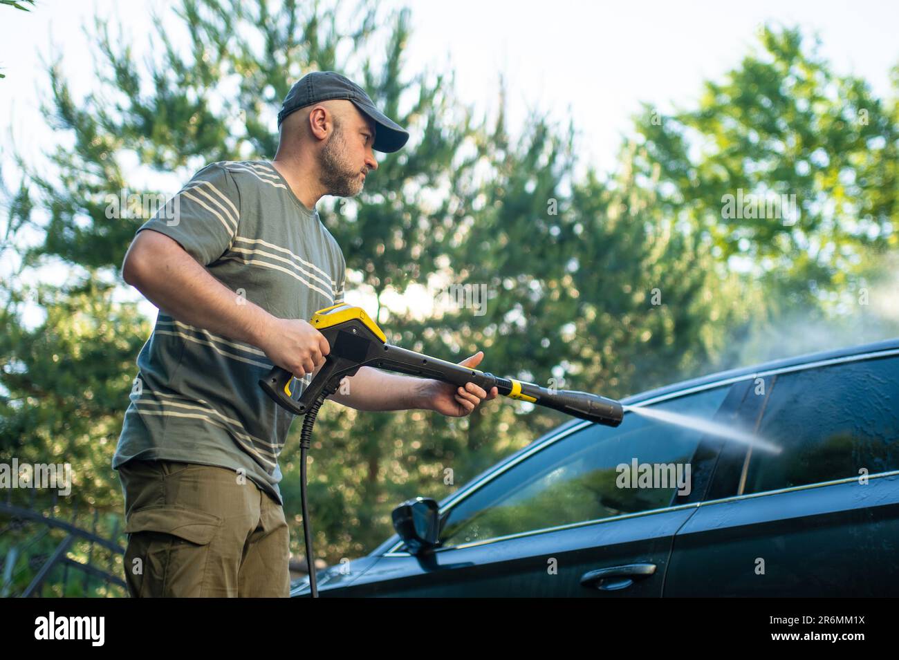 Young man using a water gun to wash his car. Male driver washing a car ...