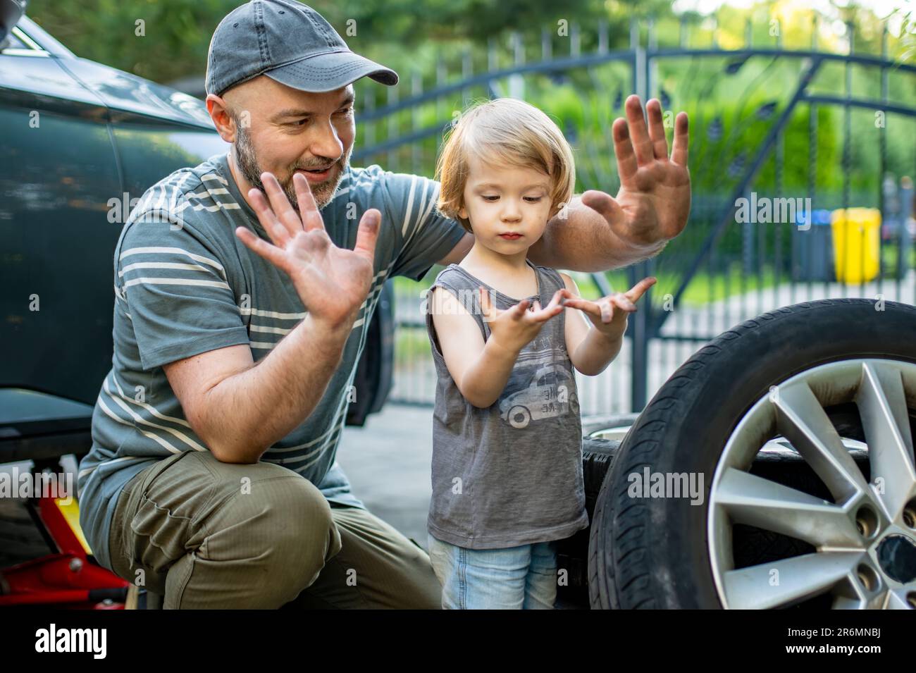Cute toddler boy helping his father to change car wheels at their ...
