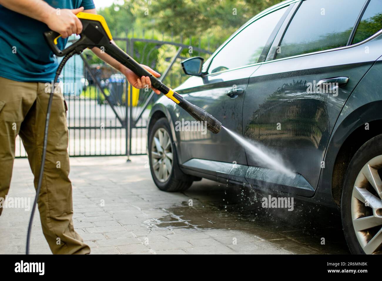 Young man using a water gun to wash his car. Male driver washing a car ...