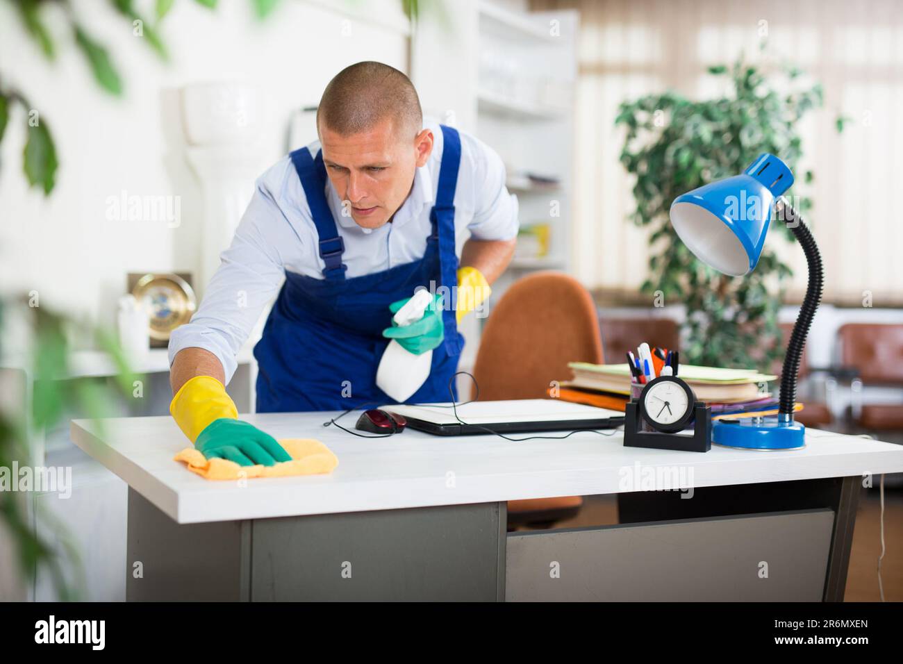 Qualified janitor dusting furniture in office with cleaning equipments ...