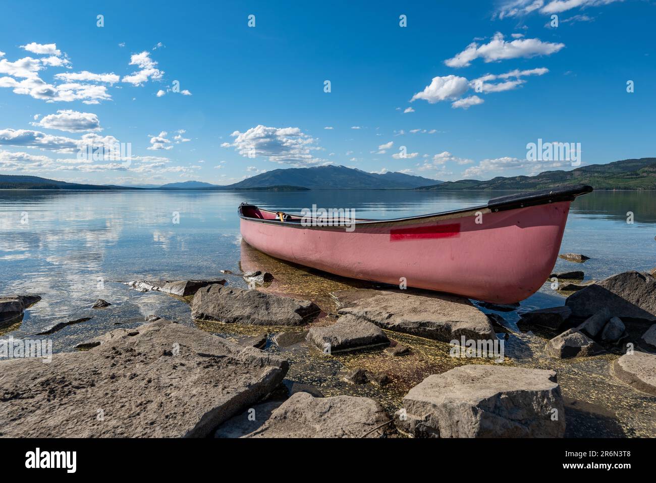 Red canoe sitting aside a rocky lake side on a beautiful blue sky ...