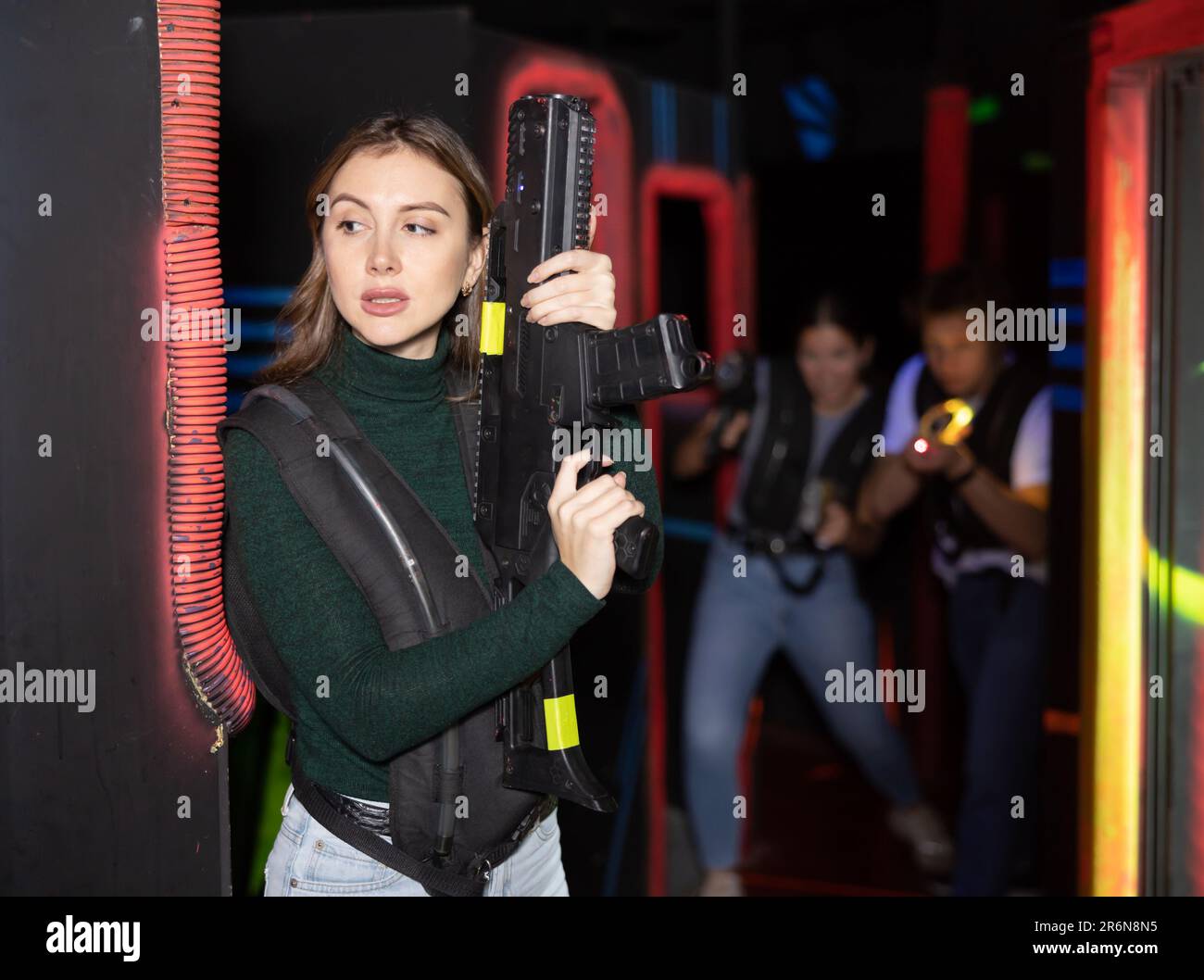 Positive girl holding laser pistol playing laser tag game with friends ...