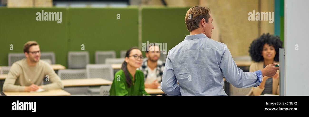 Rear view of a male business coach or speaker pointing at flip chart ...