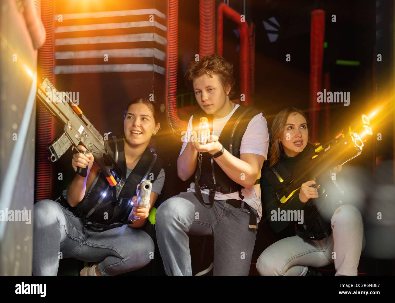 Modern young people with laser pistols playing laser tag on dark ...