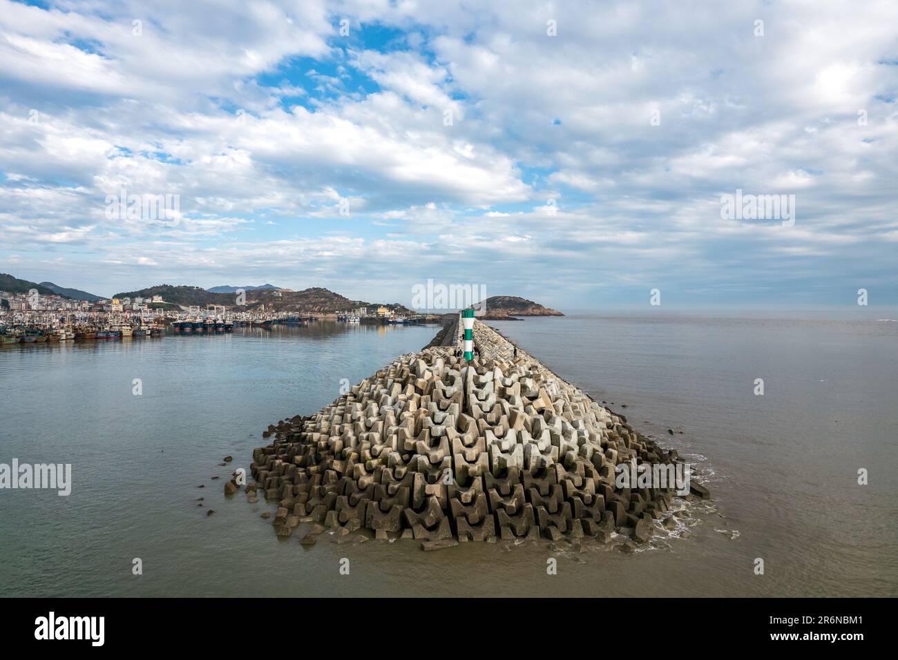 A lighthouse on the stony long pier near the coastal town at sunset ...