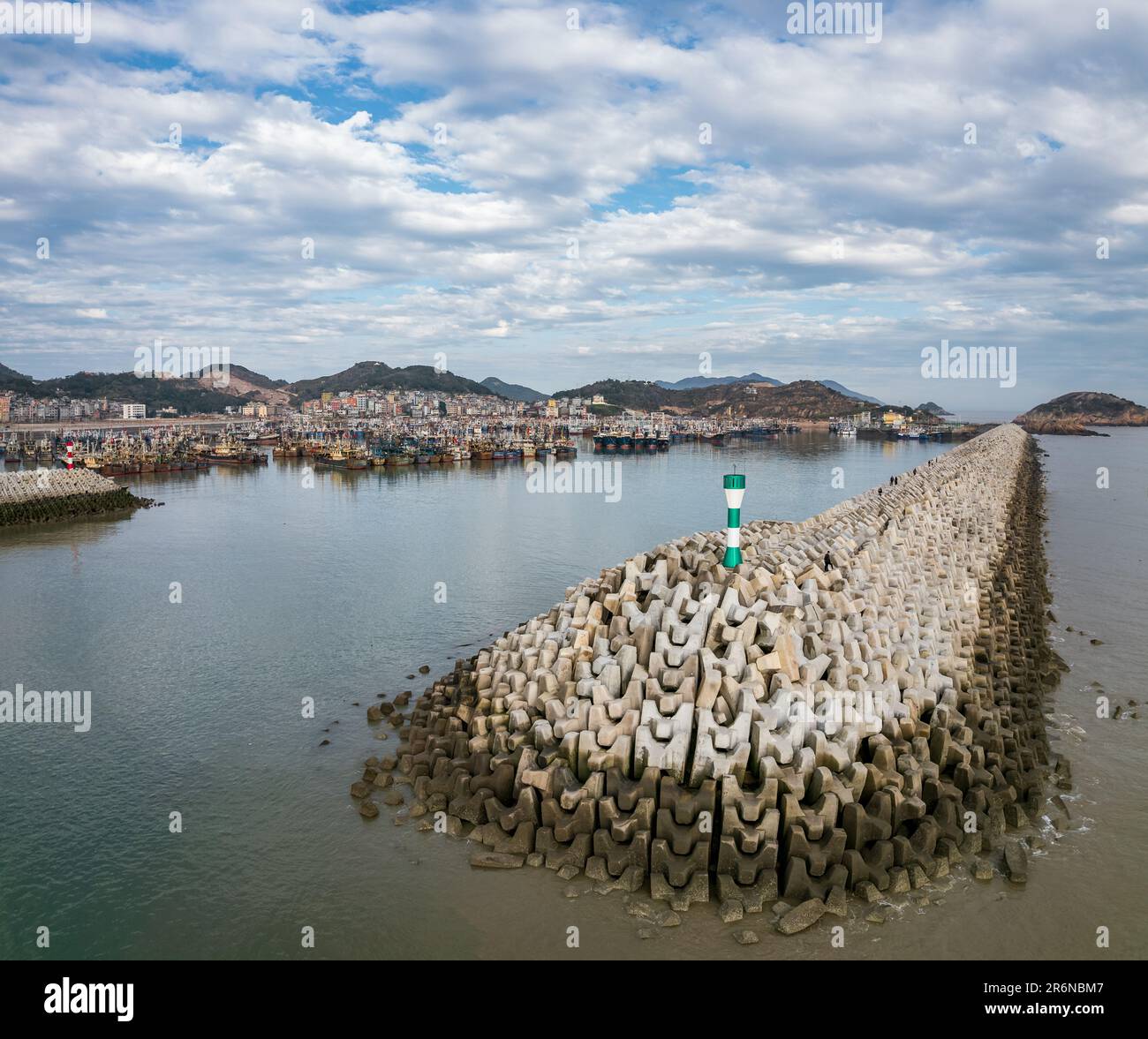 A lighthouse on the stony long pier near the coastal town at sunset ...