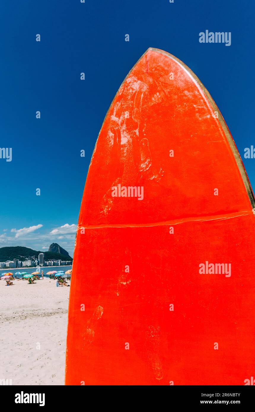 A beach scene featuring an orange surfboard sitting in the white sand ...