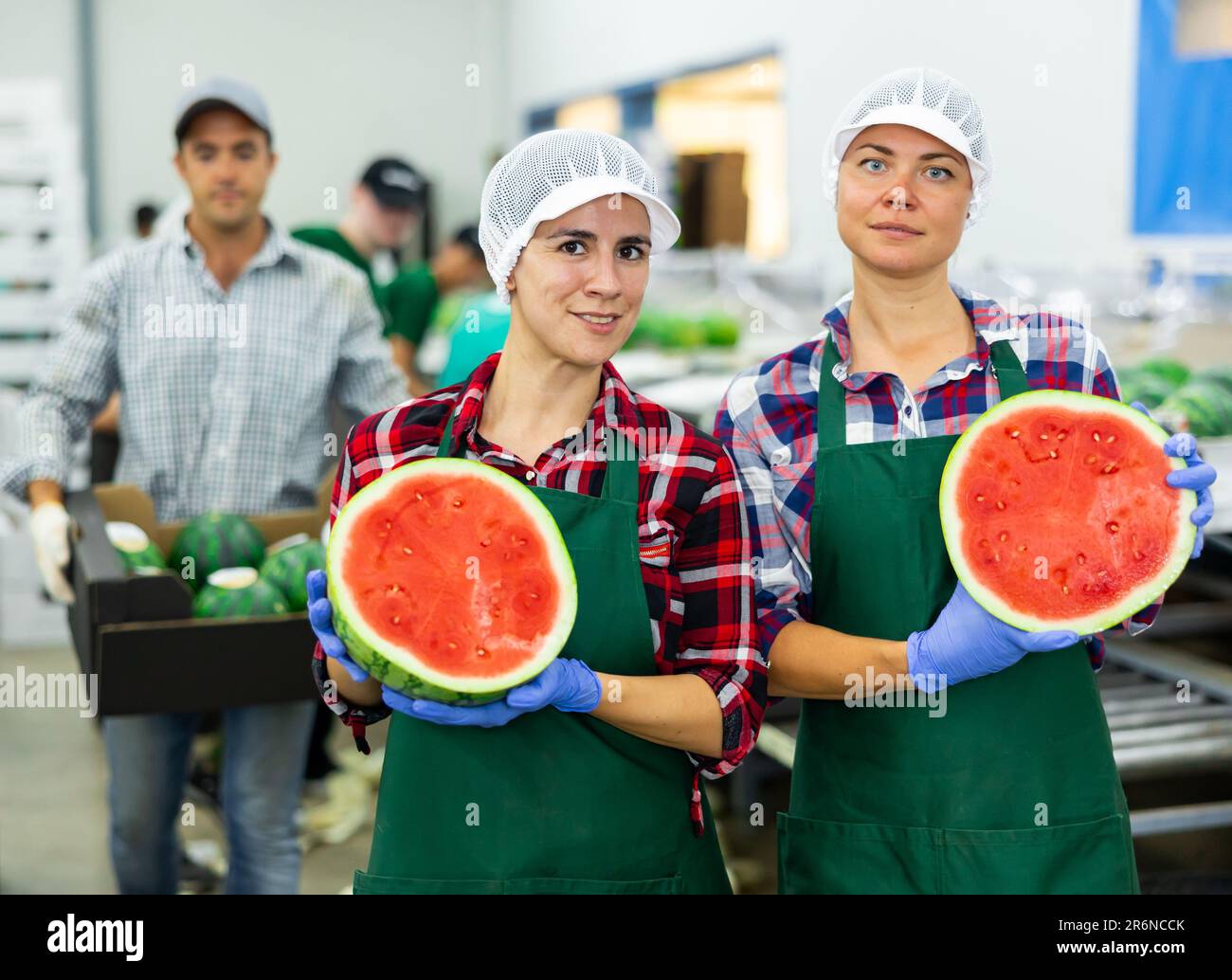 Two smiling workwomen of fruit sorting factory holding halves of ...