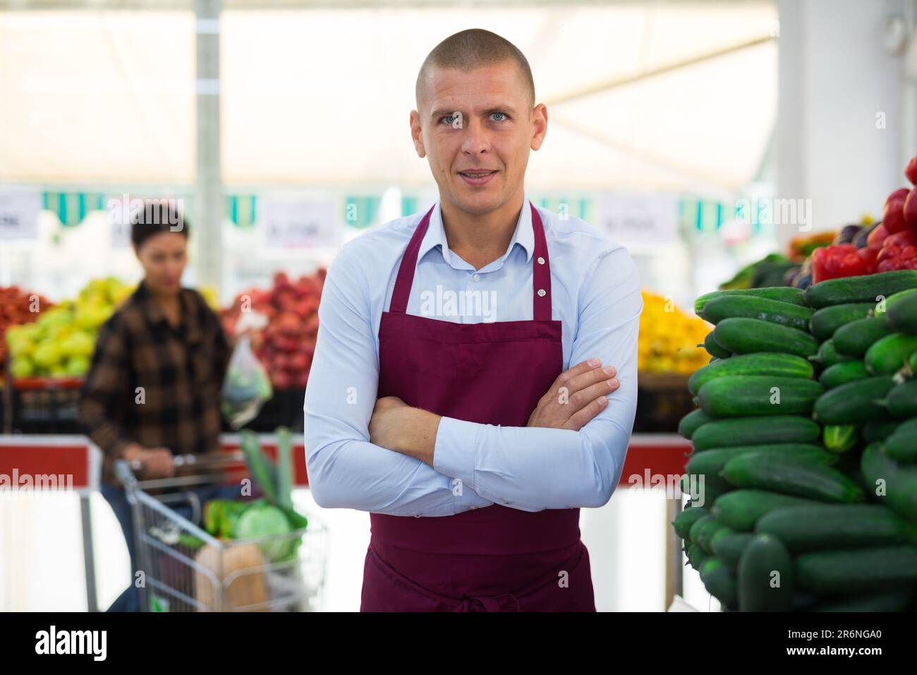 Confident greengrocery owner near shelves with fruits and vegetables ...