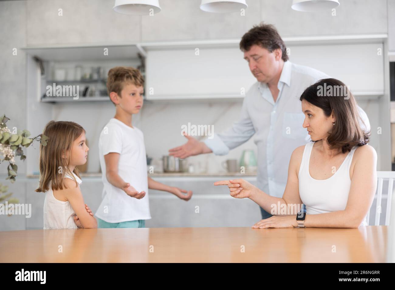 At home in kitchen, outraged mom and dad scold their son and daughter ...