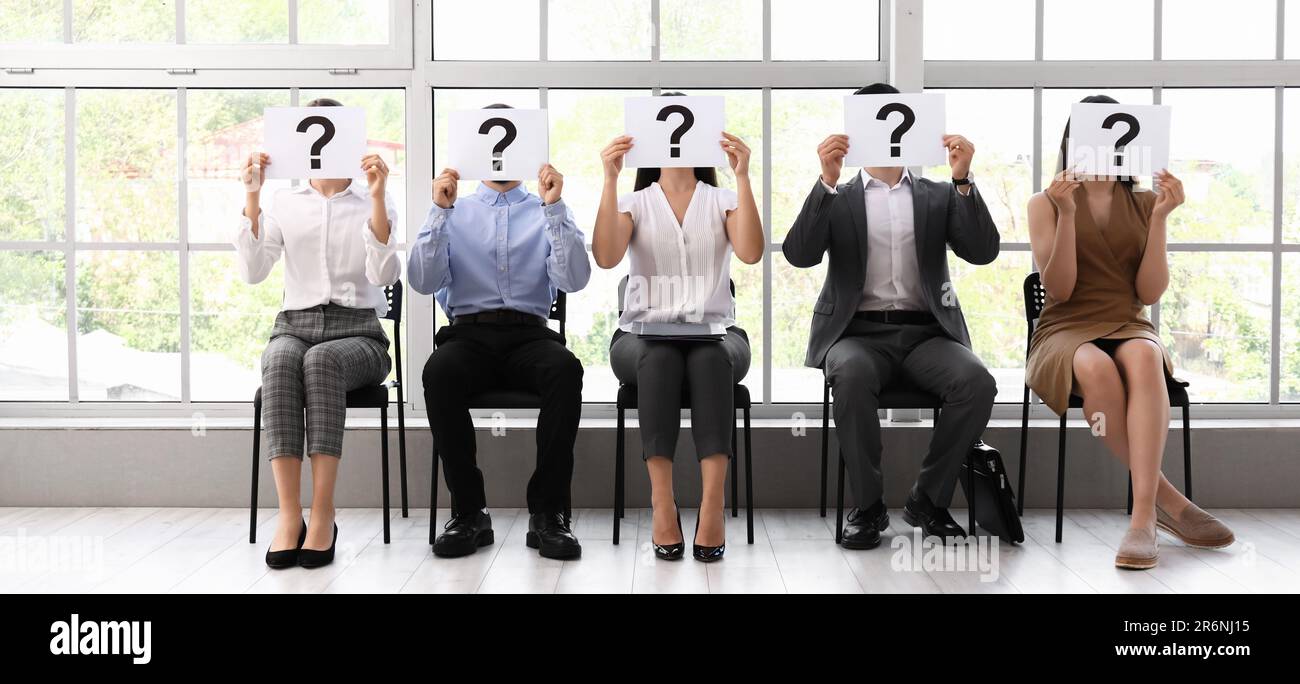 Young people hiding faces behind paper sheets with question marks while ...