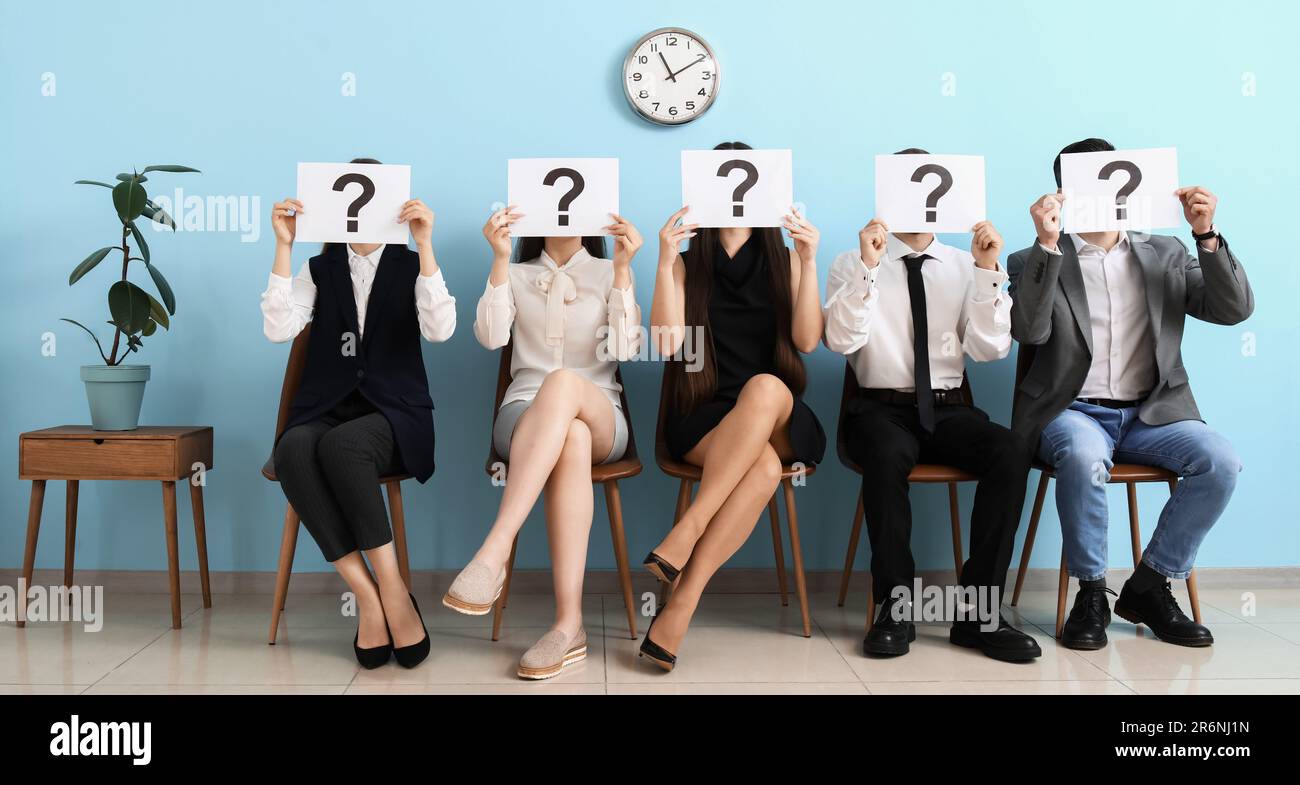 People hiding faces behind paper sheets with question marks while ...