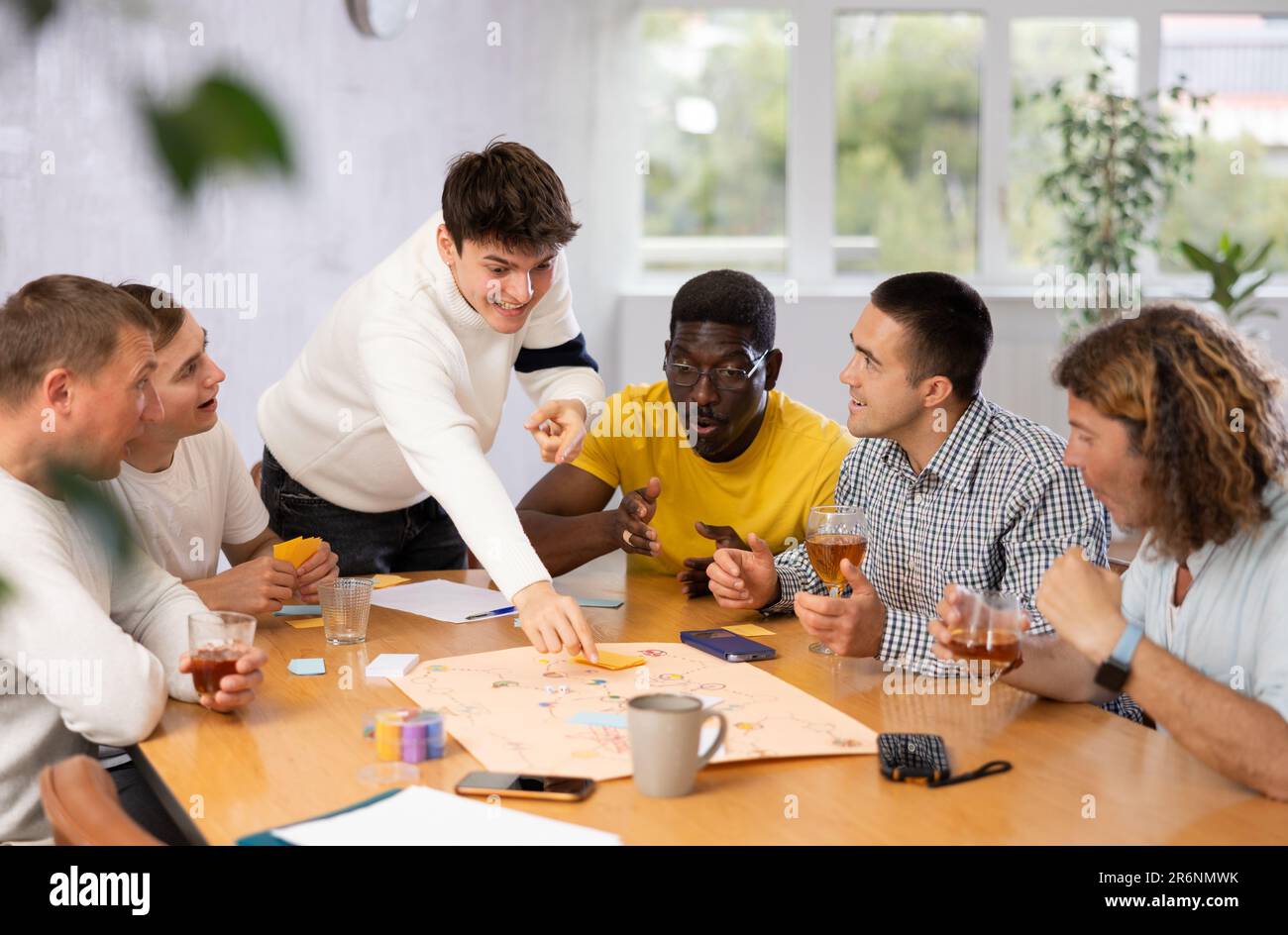 Group of enthusiastic men playing board game sitting around table Stock ...