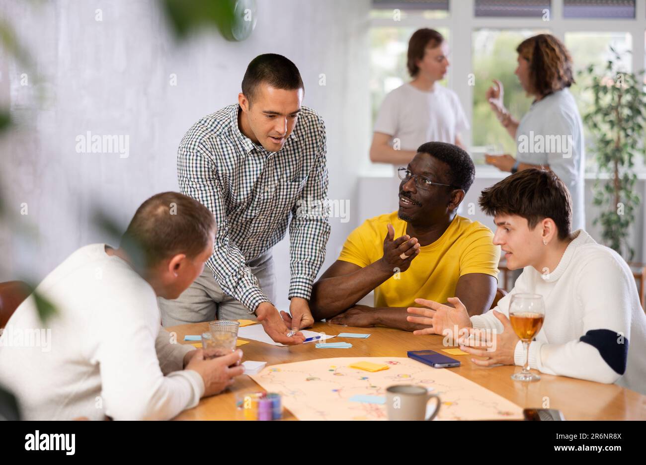 Group of enthusiastic men playing board game sitting around table Stock ...