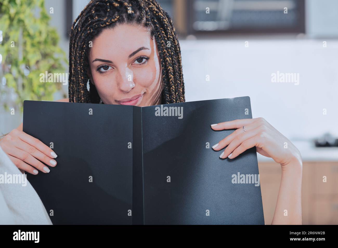 Smiling mischievously, a woman with box braids enjoys a black-cover ...