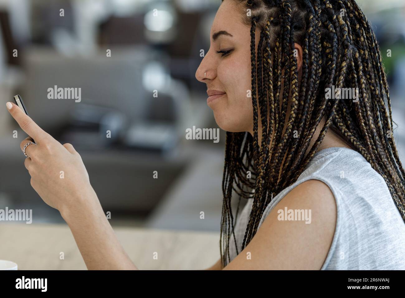 A young woman with box braids, in her kitchen, uses her smartphone for ...