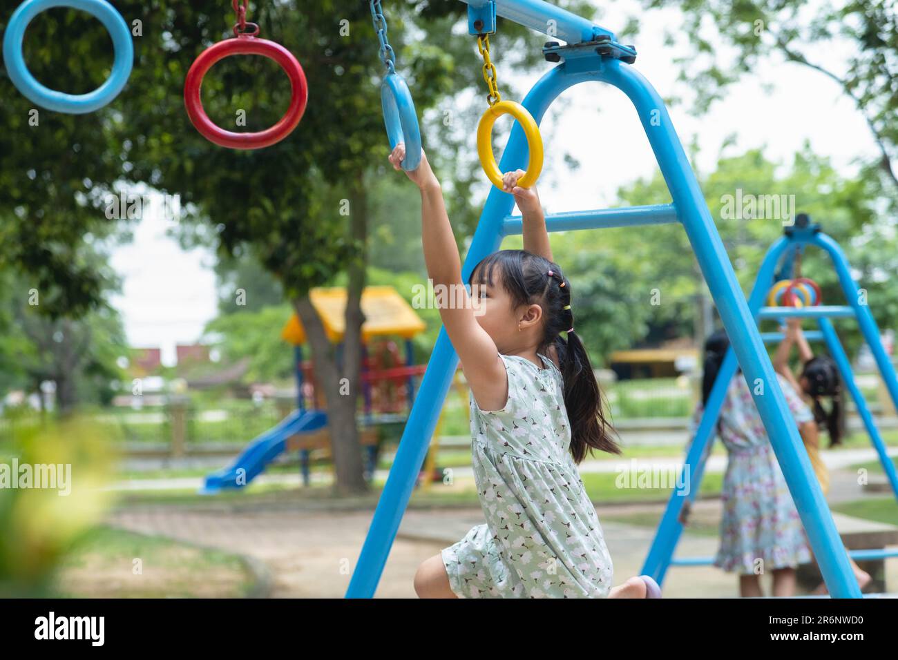 Happy girl hanging on monkey bar by hand doing exercise. Little Asian ...
