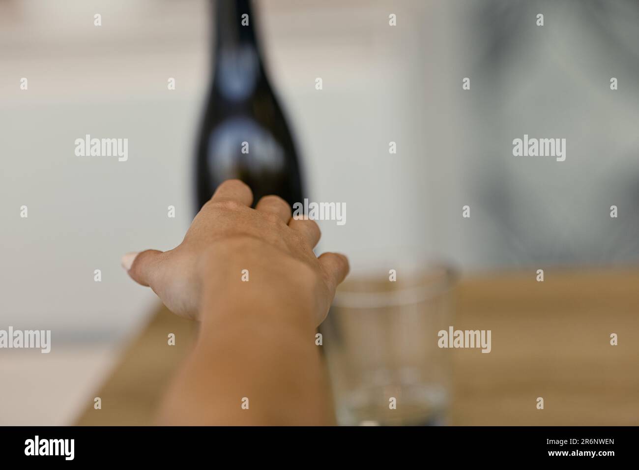 A hand in a slightly visible kitchen stretches for a craved alcohol ...