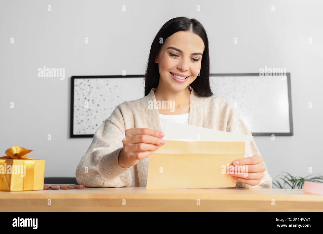 Happy woman reading greeting card at wooden table in room Stock Photo ...