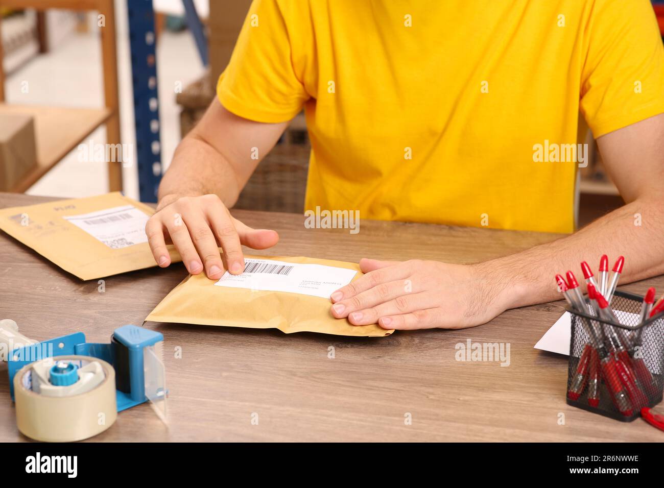 Post office worker sticking barcode on parcel at counter indoors ...