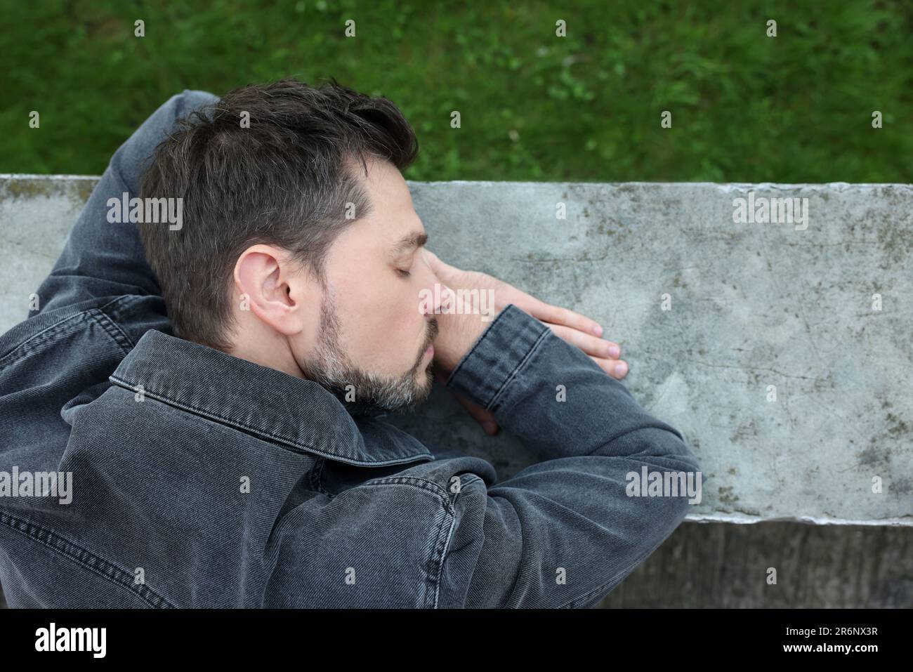 Tired man sleeping on stone parapet outdoors, top view. Space for text ...
