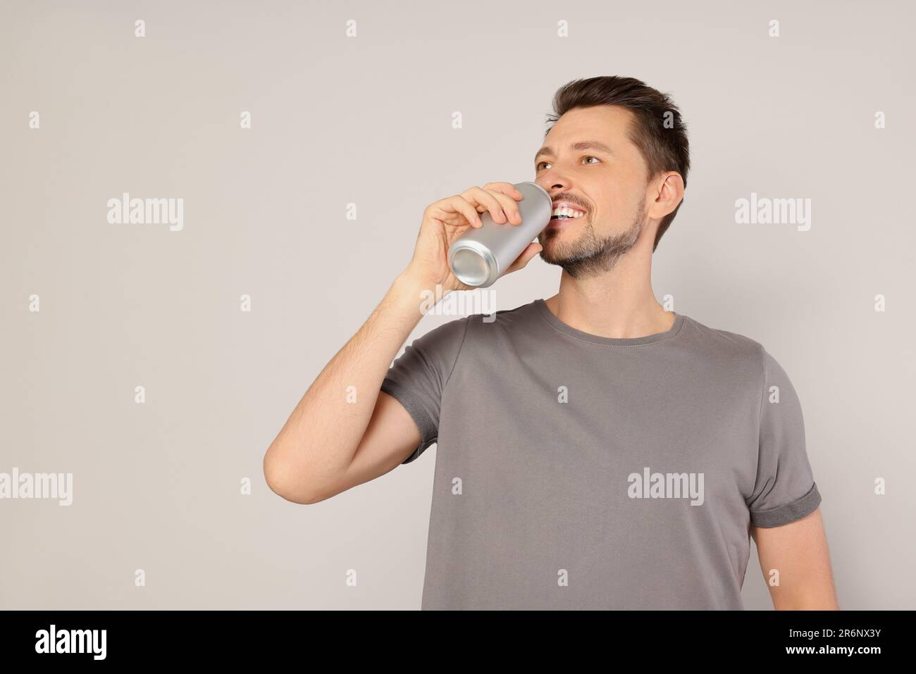 Happy man drinking from tin can on light grey background. Space for ...