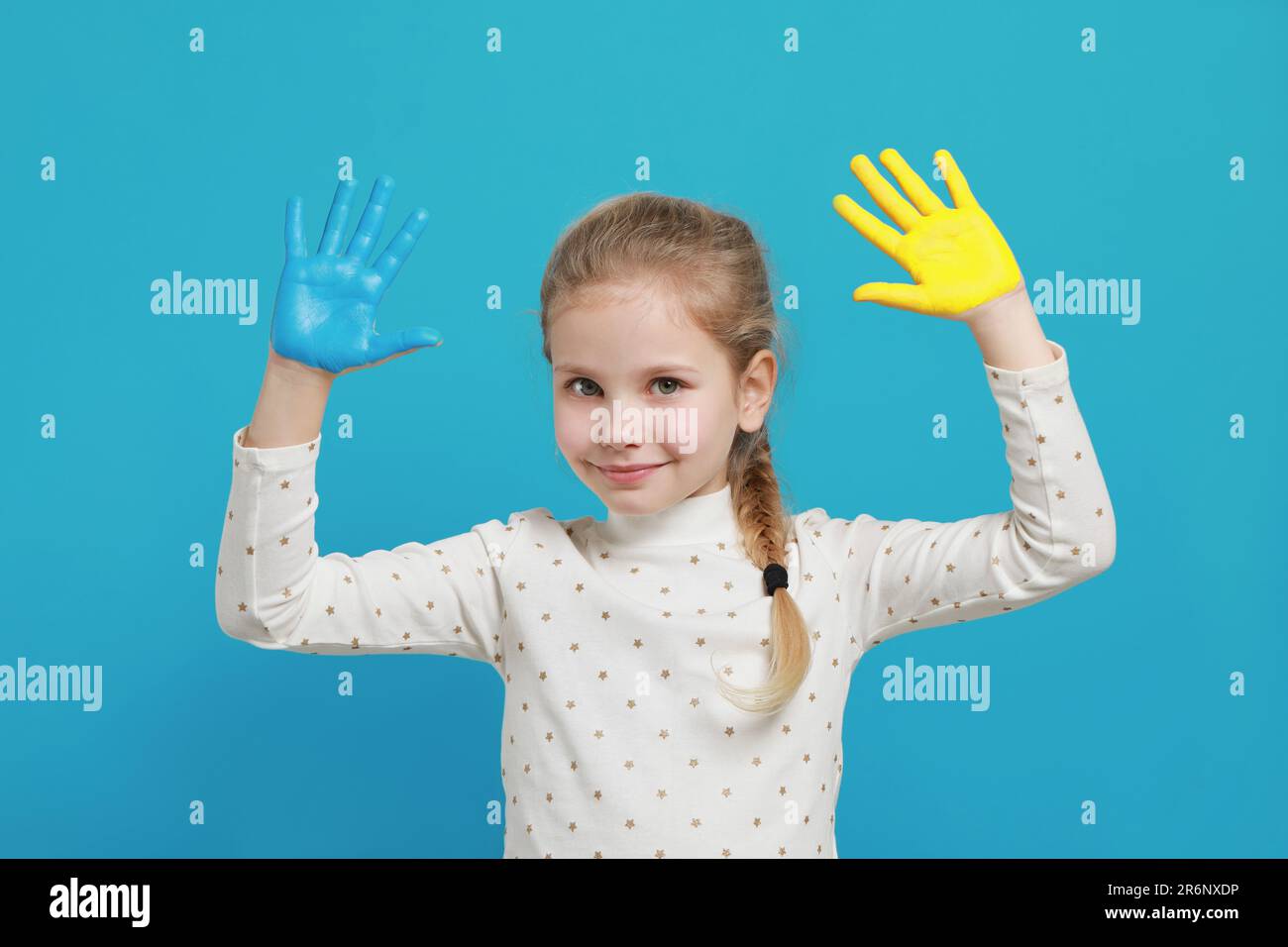 Little girl with hands painted in Ukrainian flag colors on light blue ...
