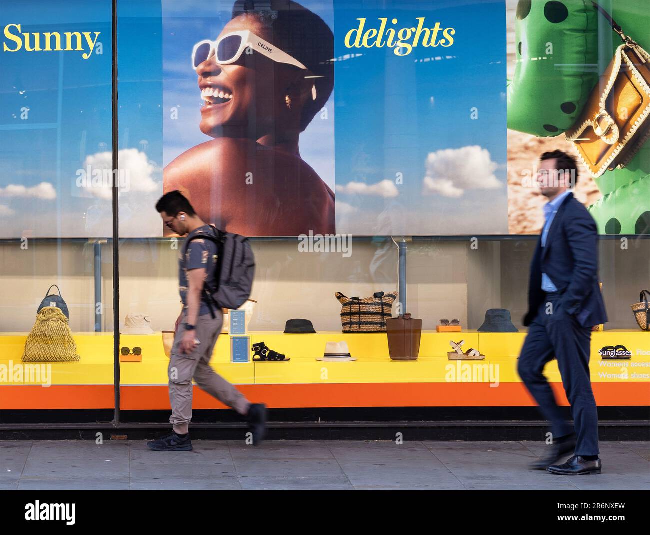 Two passers-by walking past a colourful hoarding in the window of Peter ...