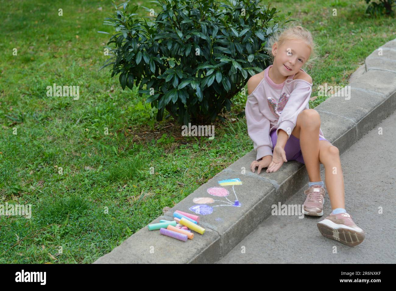 Little child sitting near drawn balloons and ukrainian flag with chalk on curb outdoors, space ...