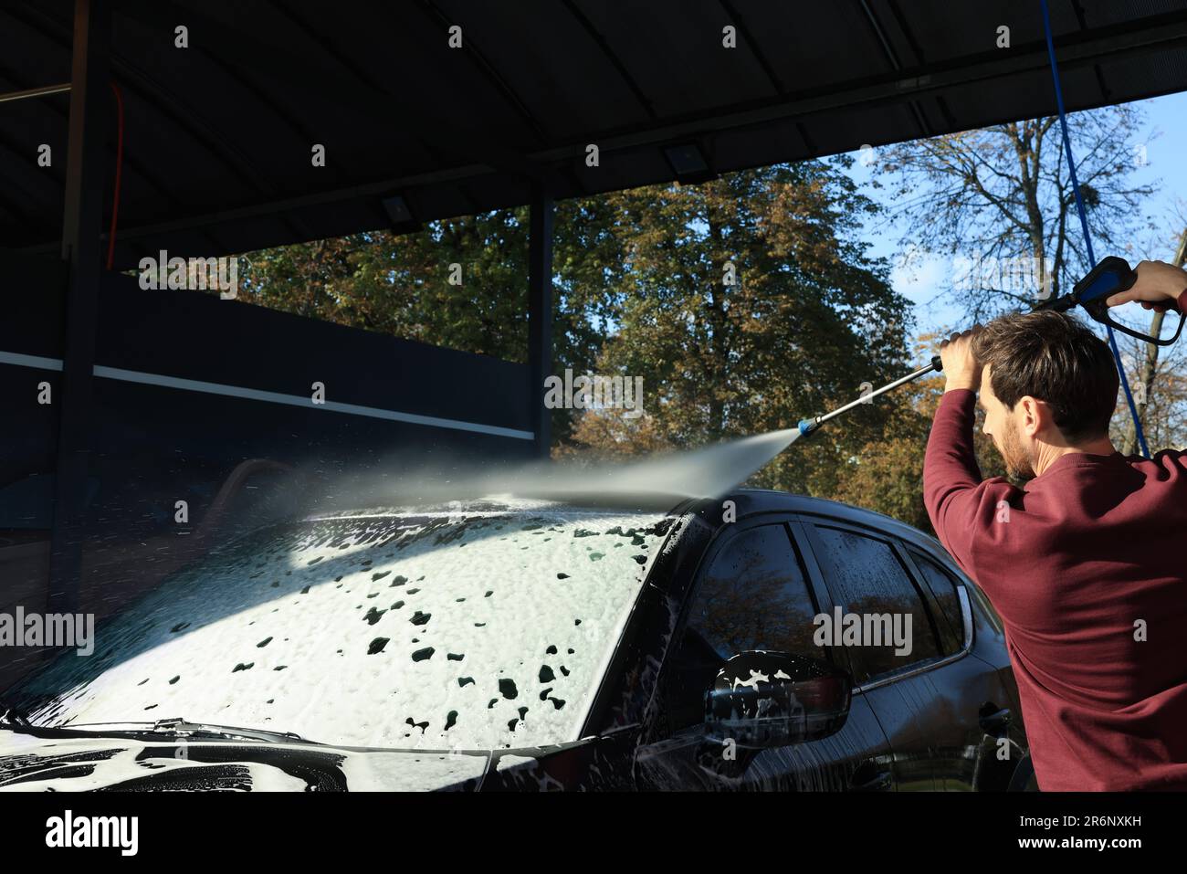 Worker washing auto with high pressure water jet at outdoor car wash ...