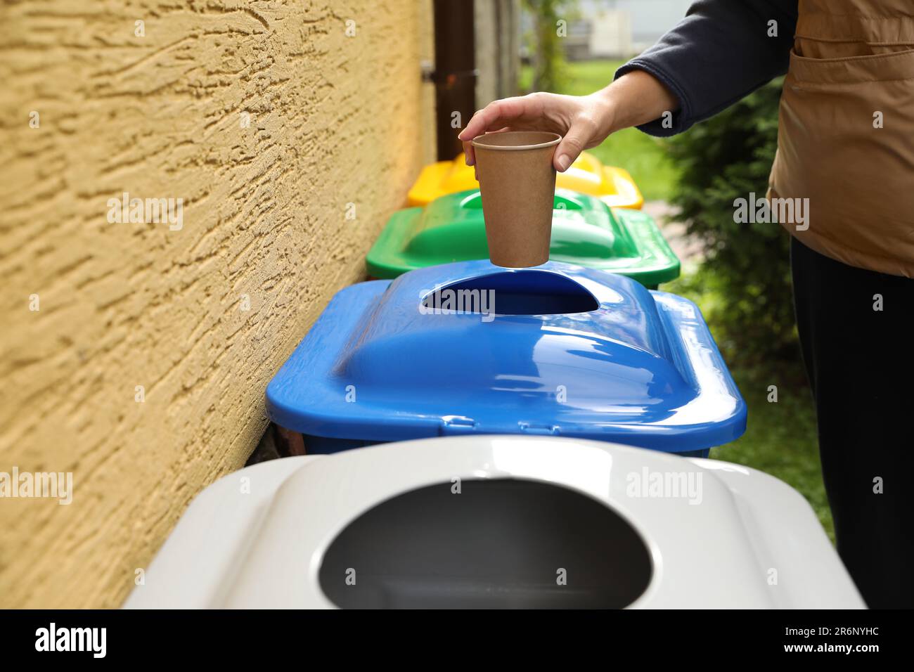 Woman throwing paper coffee cup into recycling bin outdoors, closeup ...