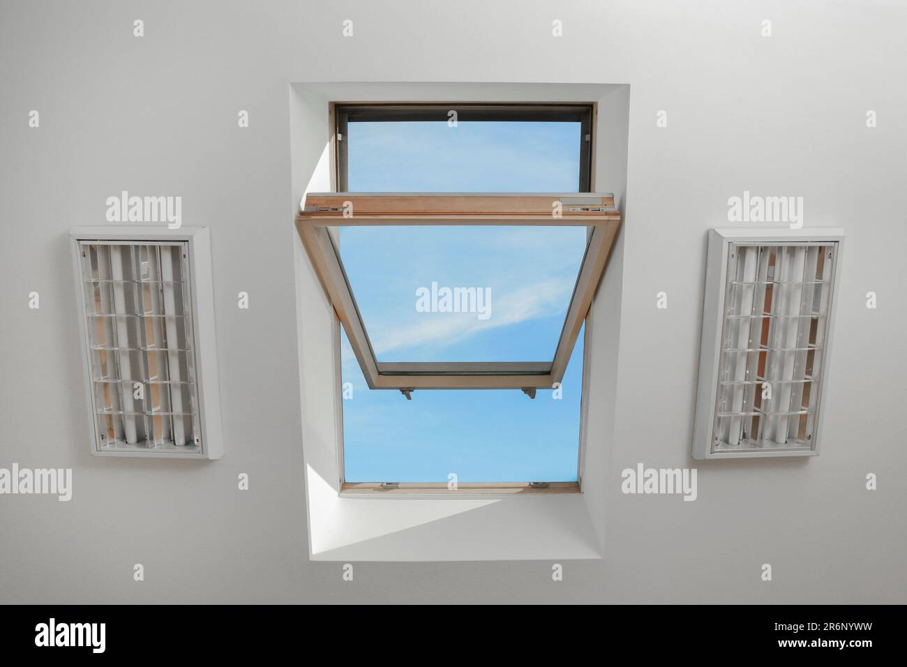 Open skylight roof window on slanted ceiling in attic room, bottom view ...