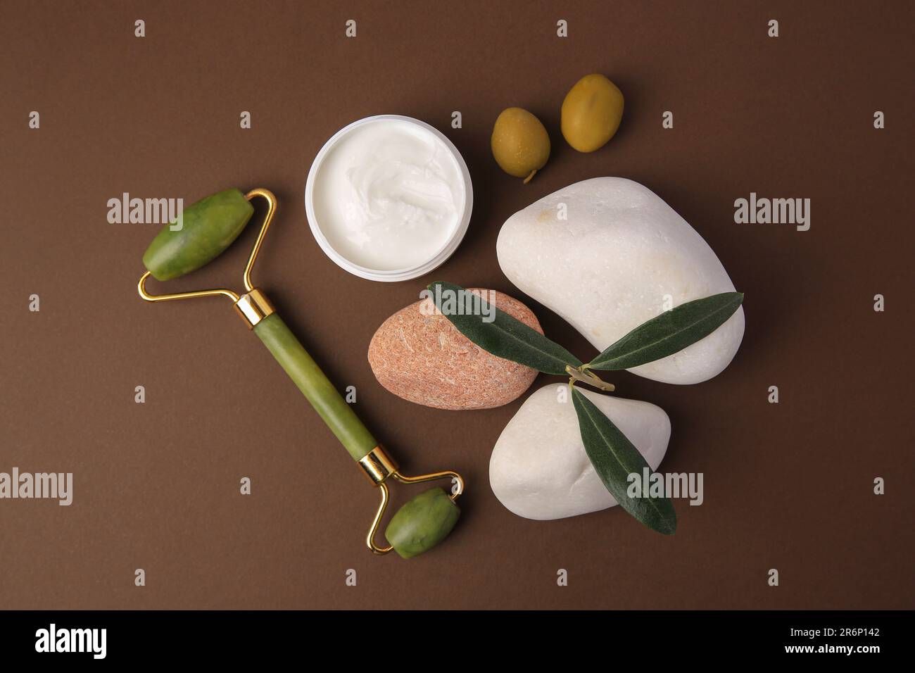 Flat lay composition with jar of cream, face roller and stones on brown ...