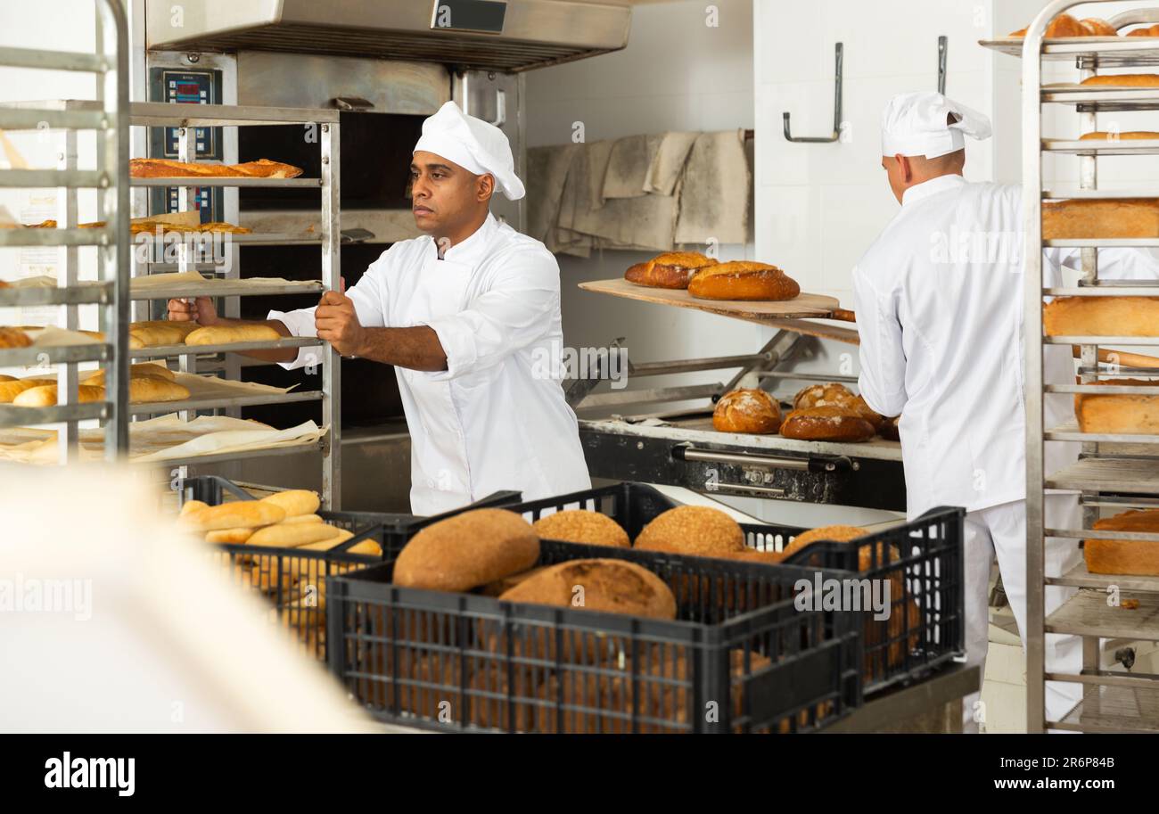 men in chefs uniform with bread in shovel and trolley in bakehouse ...