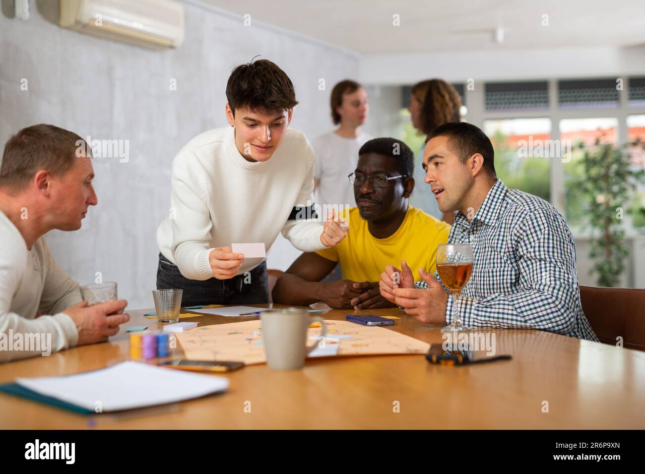 Group of enthusiastic men playing board game sitting around table Stock ...