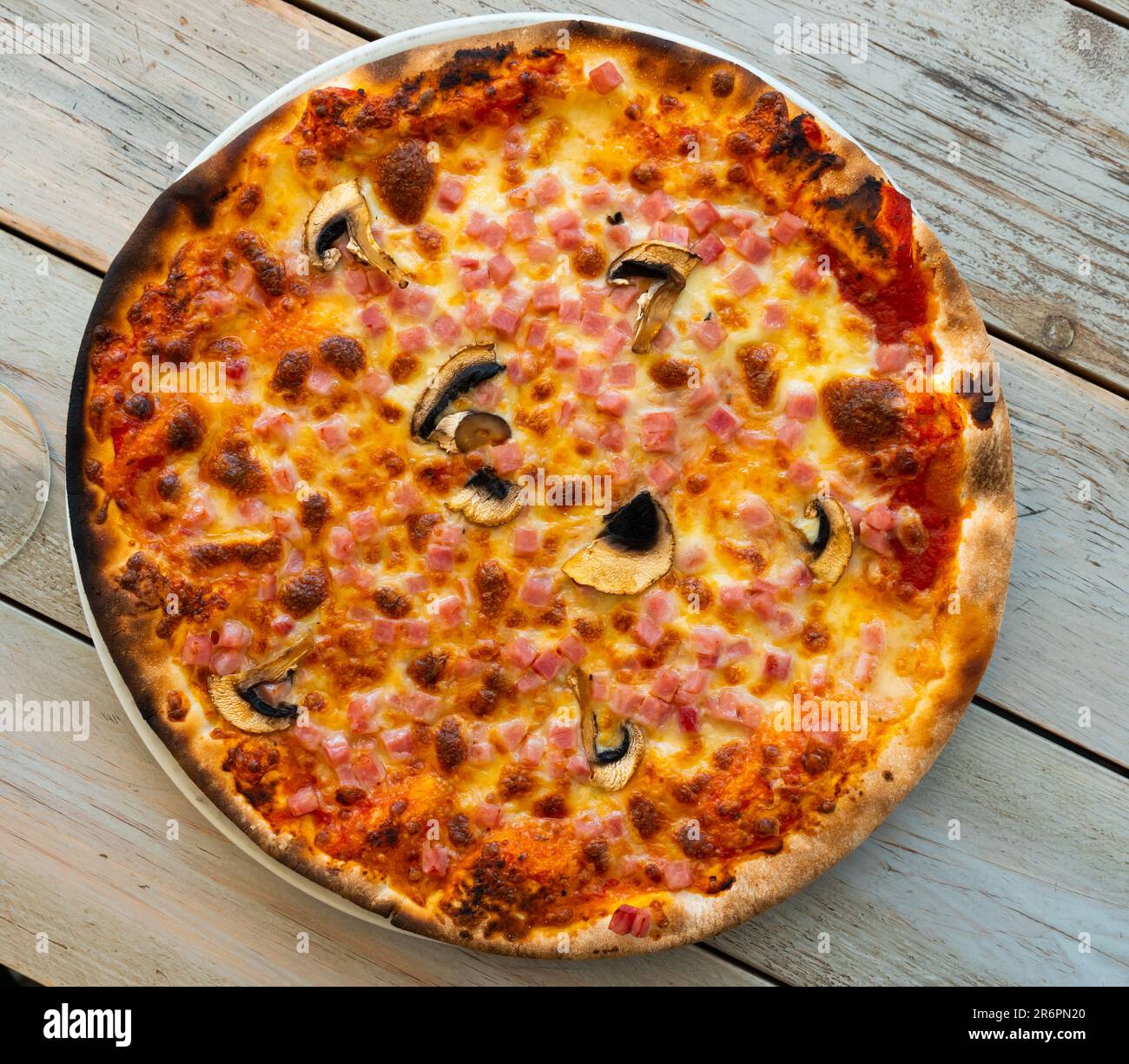 On plate is small round pizza with cubes of ham and slices of mushrooms ...