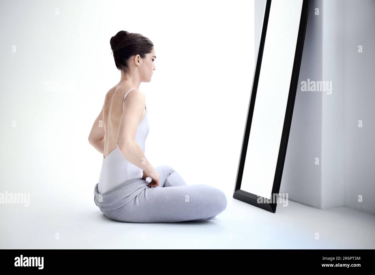 Female ballerina stretching by a mirror in a studio before a dance ...
