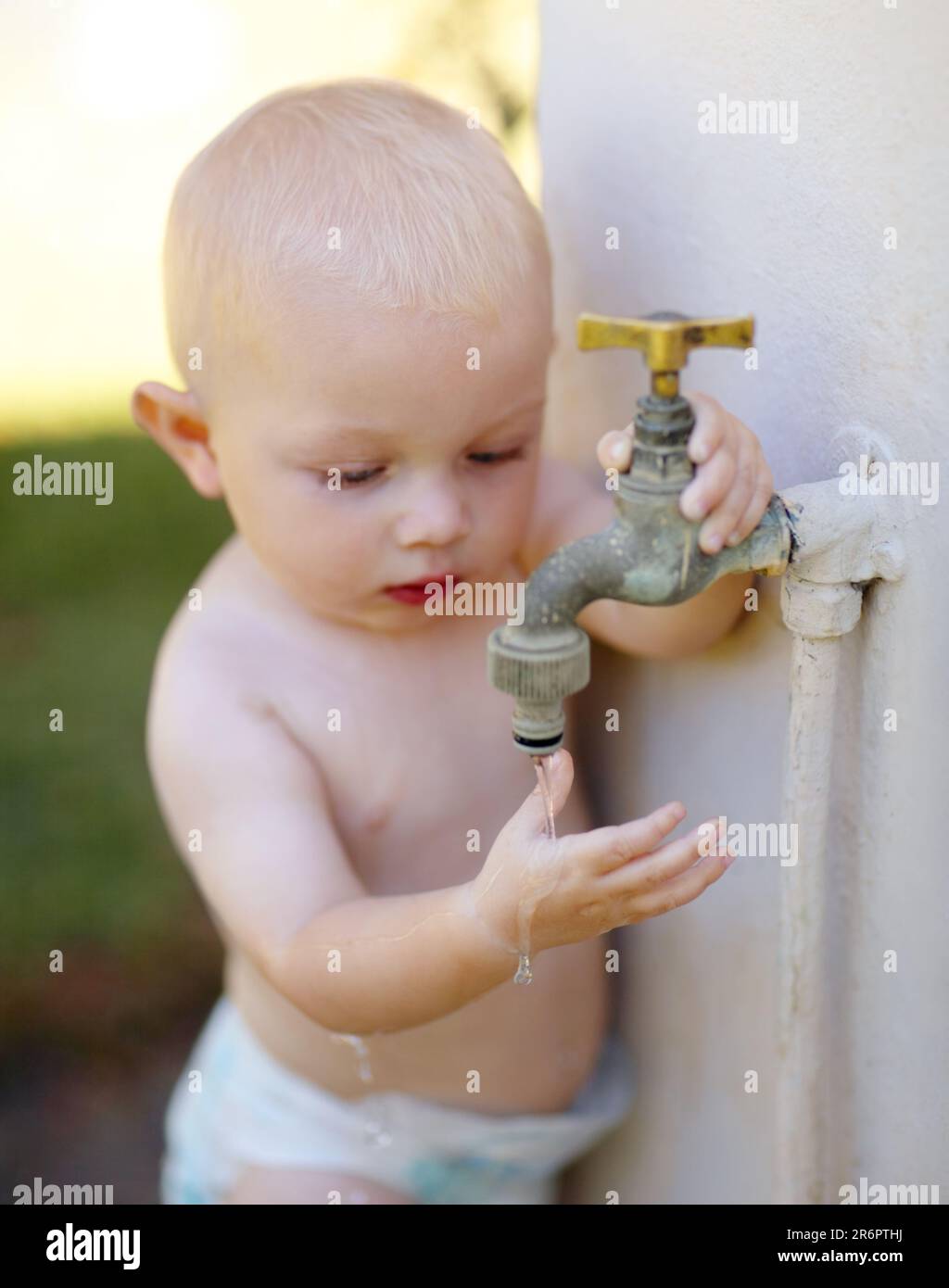Outdoor, water and a baby playing at a tap in a summer garden at home ...