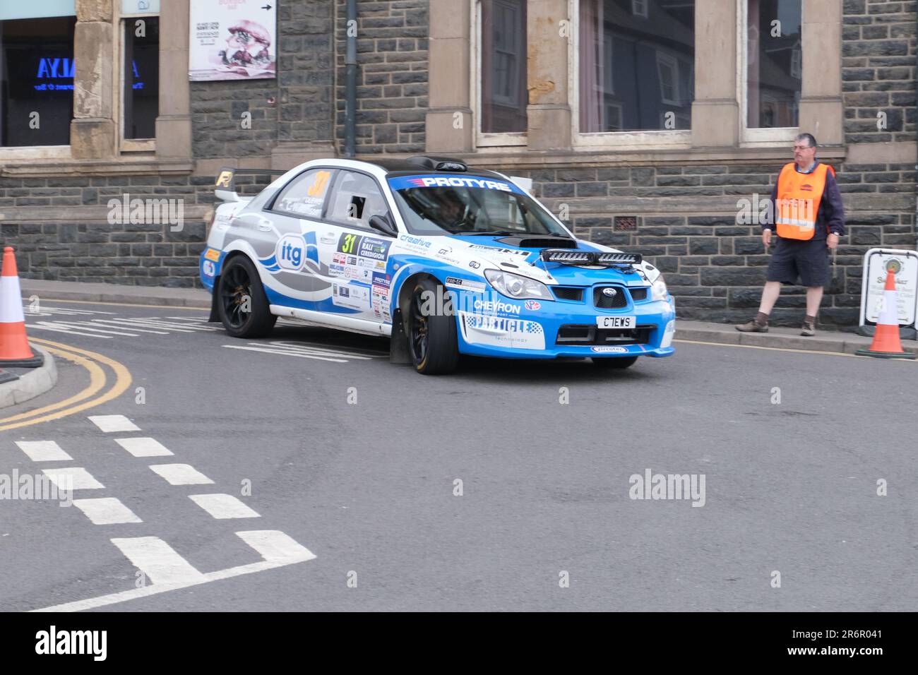 blue rally car coming around a corner with a racing marshall in the ...