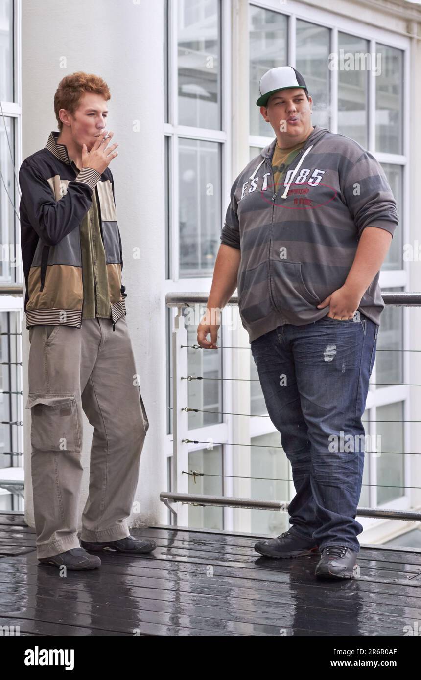 Teen men, friends and smoking outside education and school building ...