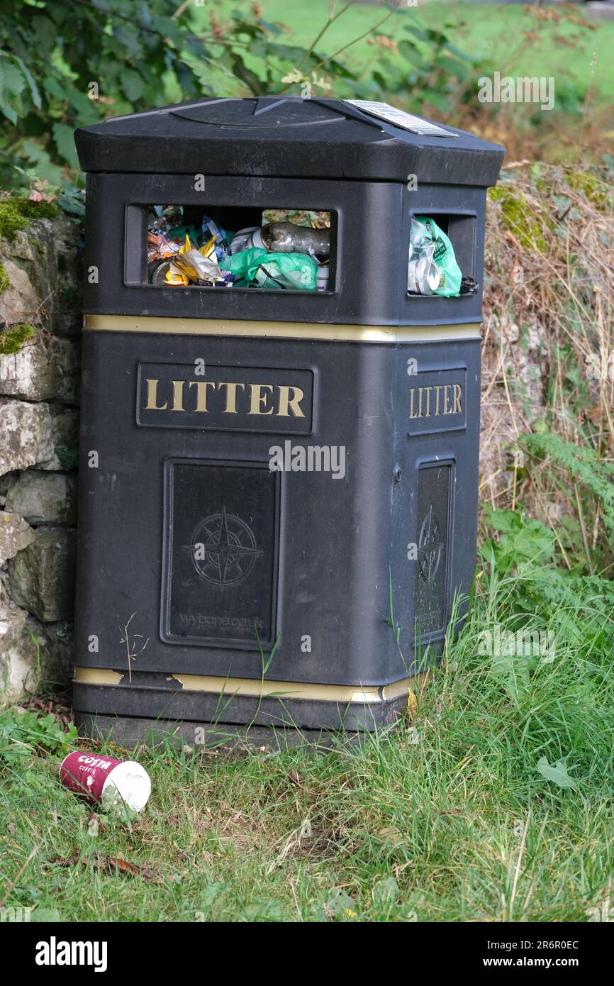 A black council litter bin with gold writing that is full to and ...